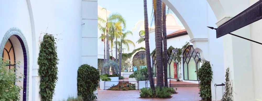 Paseo Nuevo courtyard with white arches, palm trees, and tiled pathways ...